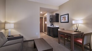 Um espaço compacto para viver com sofá, mesa de jantar com cadeiras, área de cozinha com micro-ondas e um quadro na parede.