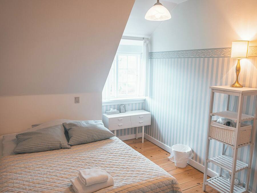 Quarto com cama, mesa de cabeceira, abajur e janela.