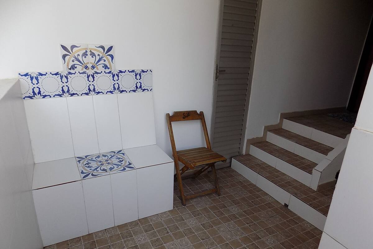 Uma escadaria com ladrilhos estampados em branco e castanho leva a um patamar. Uma cadeira de madeira está posicionada no patamar.
