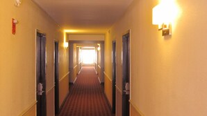 Corredor de hotel com piso em carpete, portas em ambos os lados e luminárias fixadas na parede.