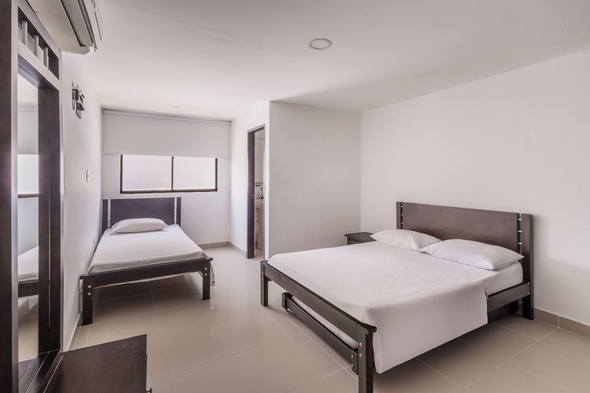 Quarto de hotel com duas camas, uma mesa e uma janela grande.