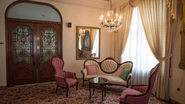 Um quarto com carpete estampado, um candelabro, um sofá e duas poltronas.