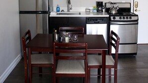 Cozinha compacta com geladeira, micro-ondas, fogão e pia. Há uma mesa de jantar com cadeiras e uma luminária no teto.