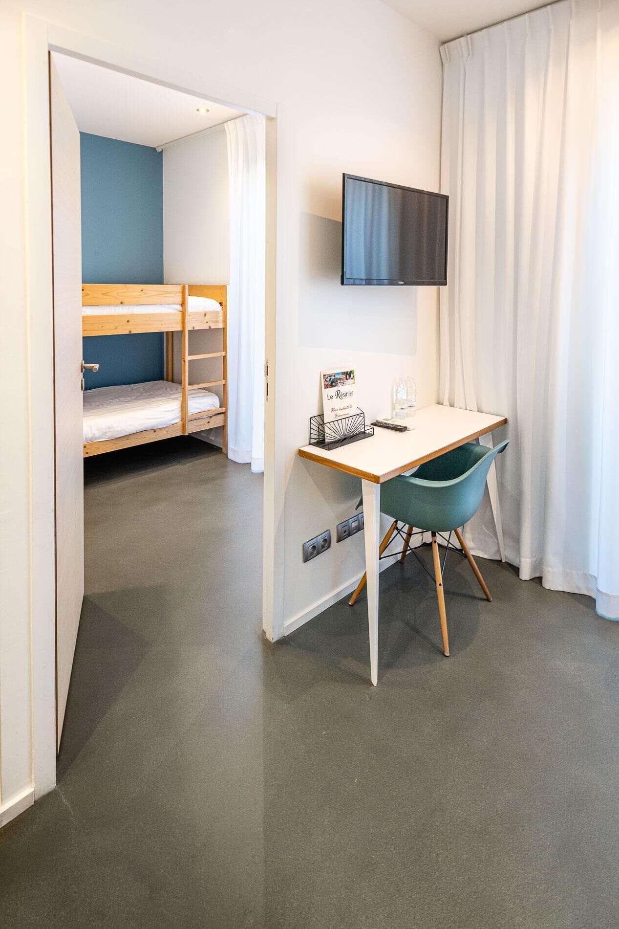 Quarto com beliche, escrivaninha com cadeira, televisão de tela plana e janela com cortinas.