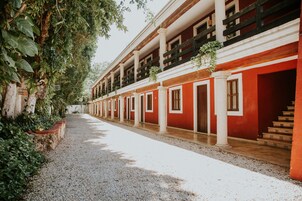 Um edifício com fachada vermelha, colunas brancas e um caminho de brita.
