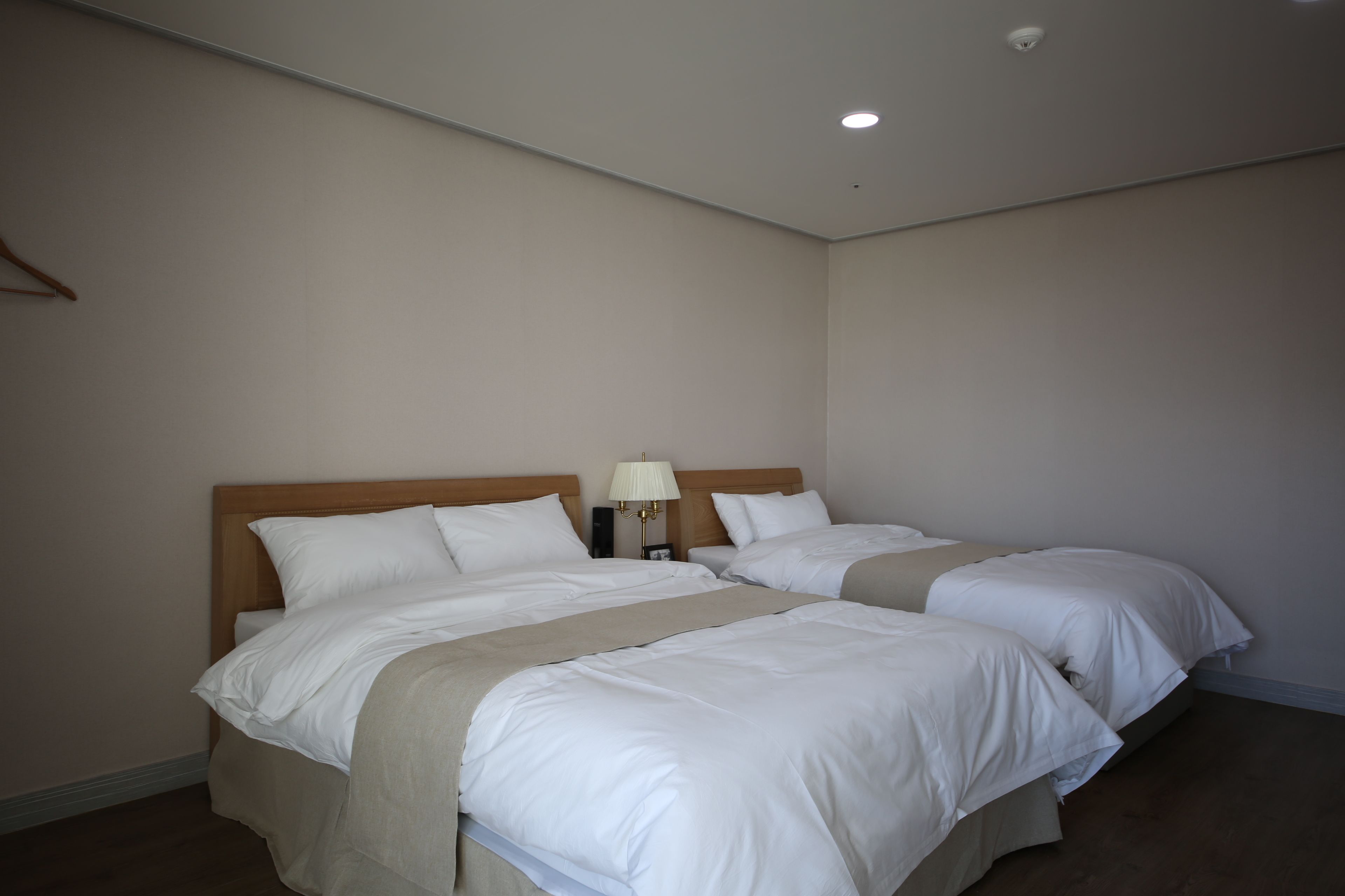 Quarto de hotel com duas camas, uma mesa de cabeceira com abajur e cabeceira de madeira.