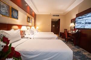 Quarto de hotel com duas camas, uma escrivaninha com cadeira, televisão e arte decorativa na parede.