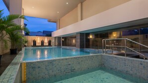 Piscina interior moderna com água cristalina, paredes azulejadas e barreira de vidro.