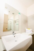 Um banheiro de hotel com uma pia grande, um espelho, um porta-toalhas e uma área de chuveiro.