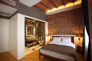 Quarto com cama grande, parede de destaque em tijolo, closet espaçoso e banheiro moderno com box de vidro.
