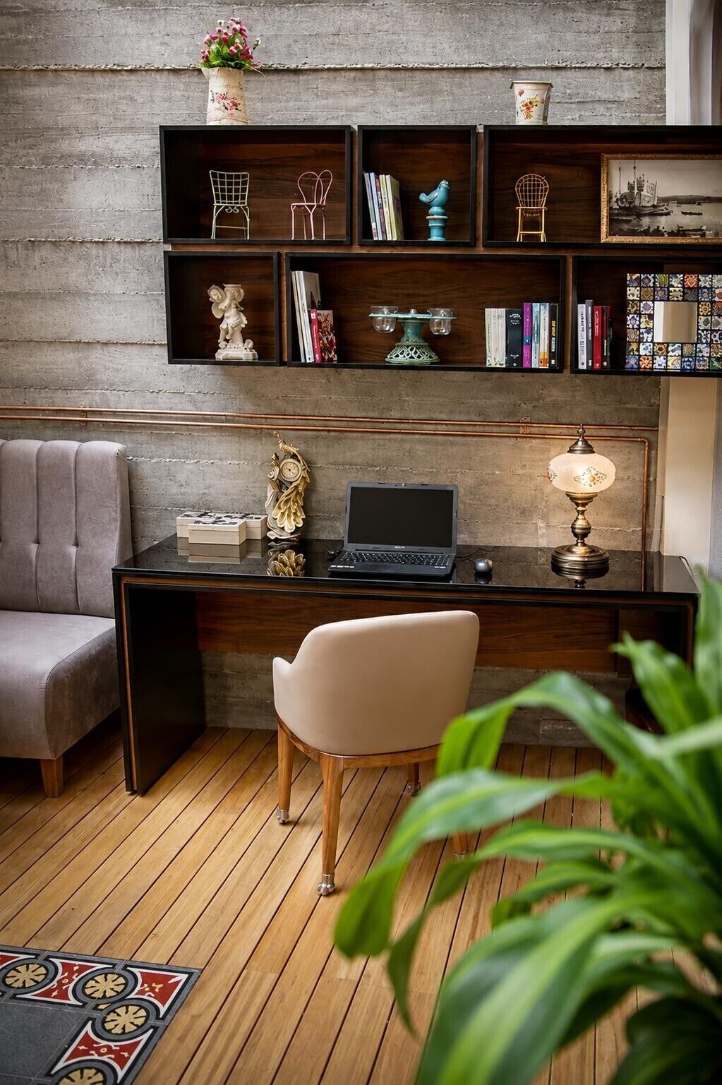 Um espaço de trabalho moderno com uma escrivaninha de madeira, um computador portátil, uma lâmpada e uma estante em frente a uma parede de concreto.