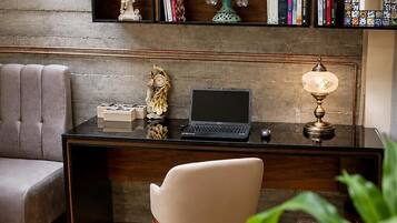 Um espaço de trabalho moderno com uma escrivaninha de madeira, um computador portátil, uma lâmpada e uma estante em frente a uma parede de concreto.