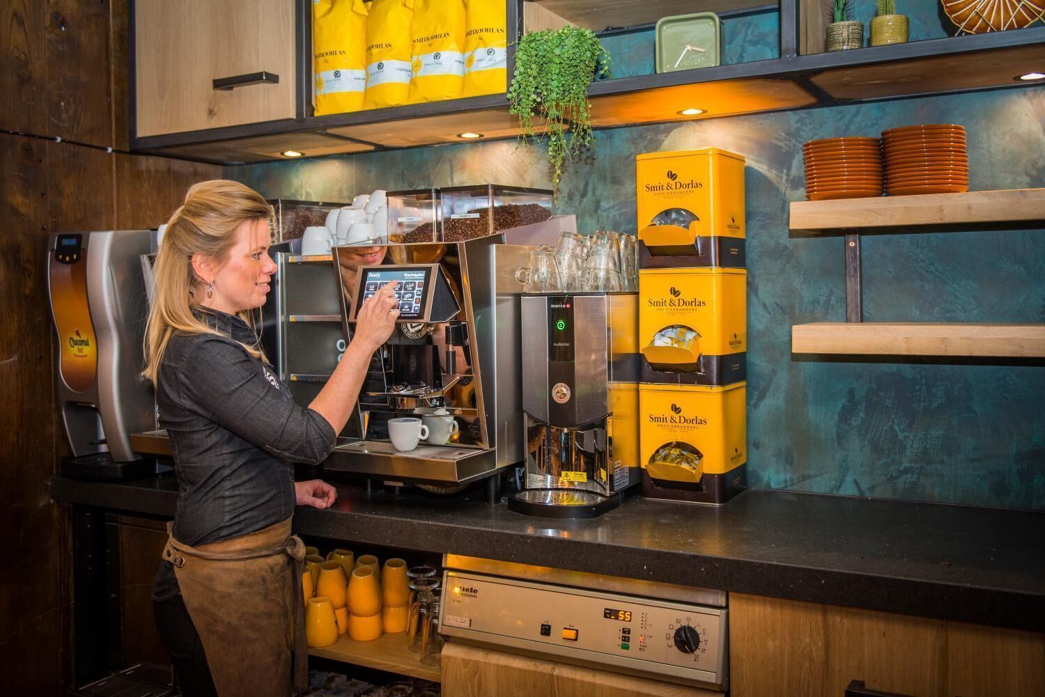 Um barista preparando café no balcão, com máquinas de café, um moedor e embalagens de café com a marca.