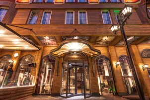 Entrada de hotel com porta giratória, fachada de madeira e iluminação decorativa.