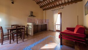 Ampla sala de estar com mesa de jantar de madeira, cadeiras, sofá vermelho e cozinha com painel de azulejos.