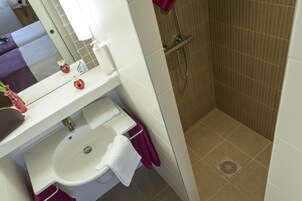 Um banheiro com pia branca, espelho, chuveiro e piso revestido de azulejos.