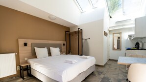 Quarto de hotel moderno com uma cama grande, uma mesinha e uma cozinha compacta.