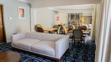 Quarto de hotel com sofá, mesa de jantar, cadeiras e um tapete estampado.