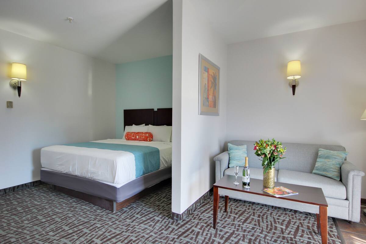 Quarto de hotel com cama, sofá, mesa de centro e luminárias fixadas na parede.
