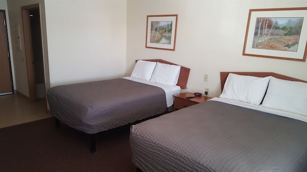 Quarto de hotel com duas camas de solteiro, uma mesinha de cabeceira de madeira, um controle remoto e duas fotos emolduradas na parede.