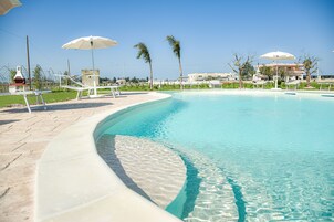 Piscina límpida com borda curva, rodeada por espreguiçadeiras e guarda-sóis.