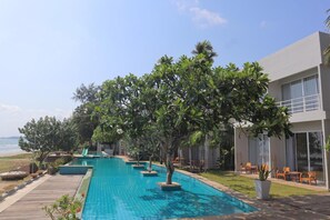 Piscina com deck de madeira, rodeada por vegetação e um edifício com janelas amplas.
