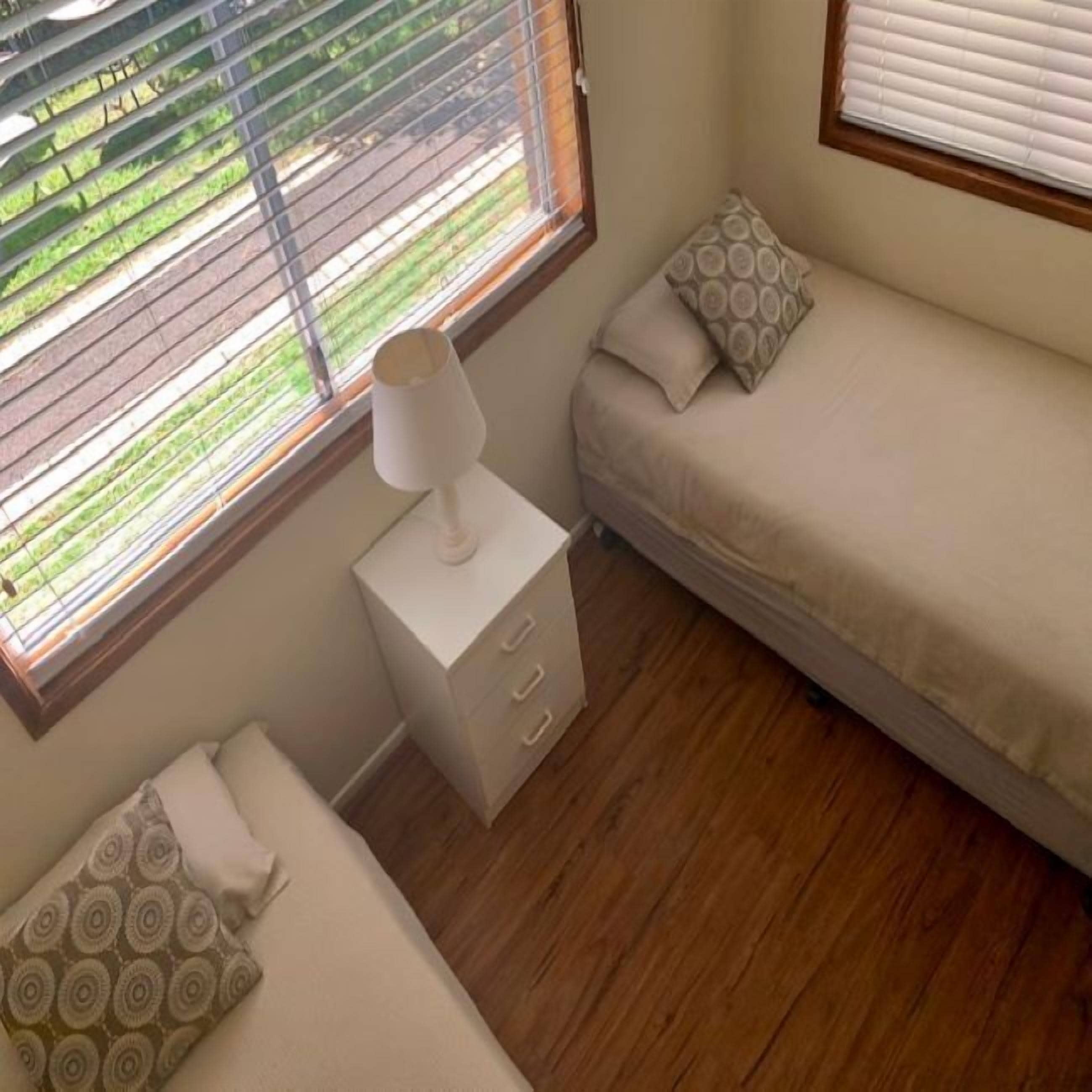 Um quarto pequeno e simples, com uma cama, mesa de cabeceira e janela com persianas.