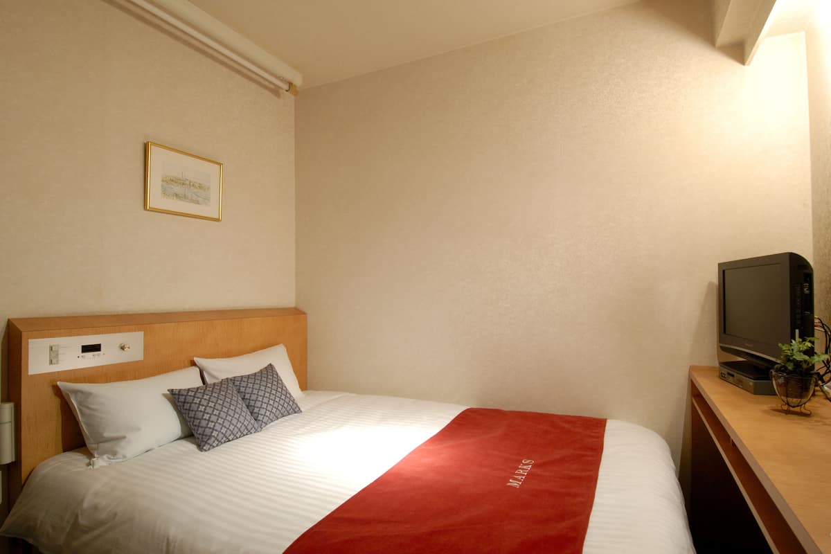Quarto de hotel com uma cama, uma televisão sobre uma mesa de cabeceira de madeira e um quadro na parede.