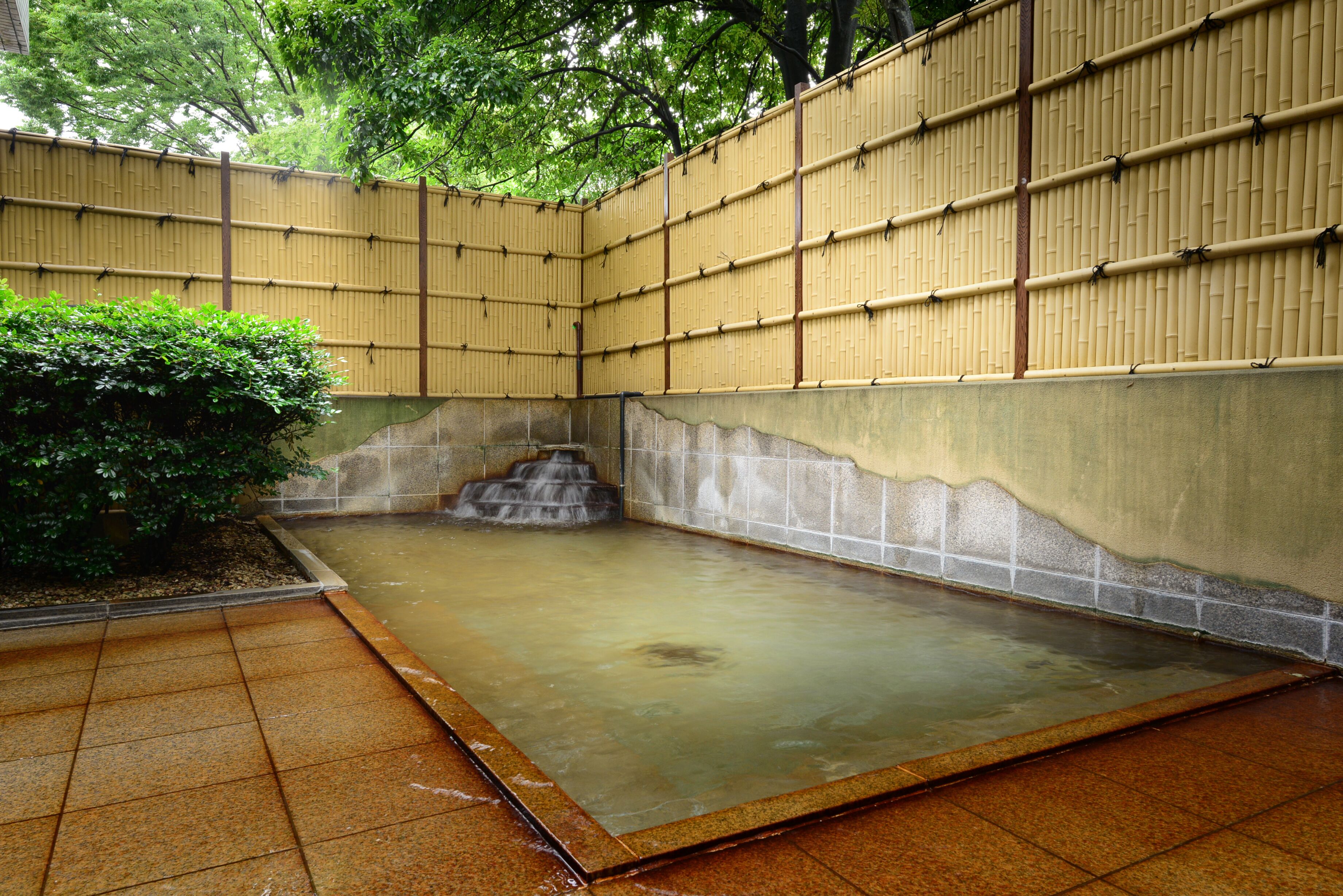Uma onsen japonesa tradicional com uma nascente quente de pedra, soalho em azulejo e paredes de bambu.