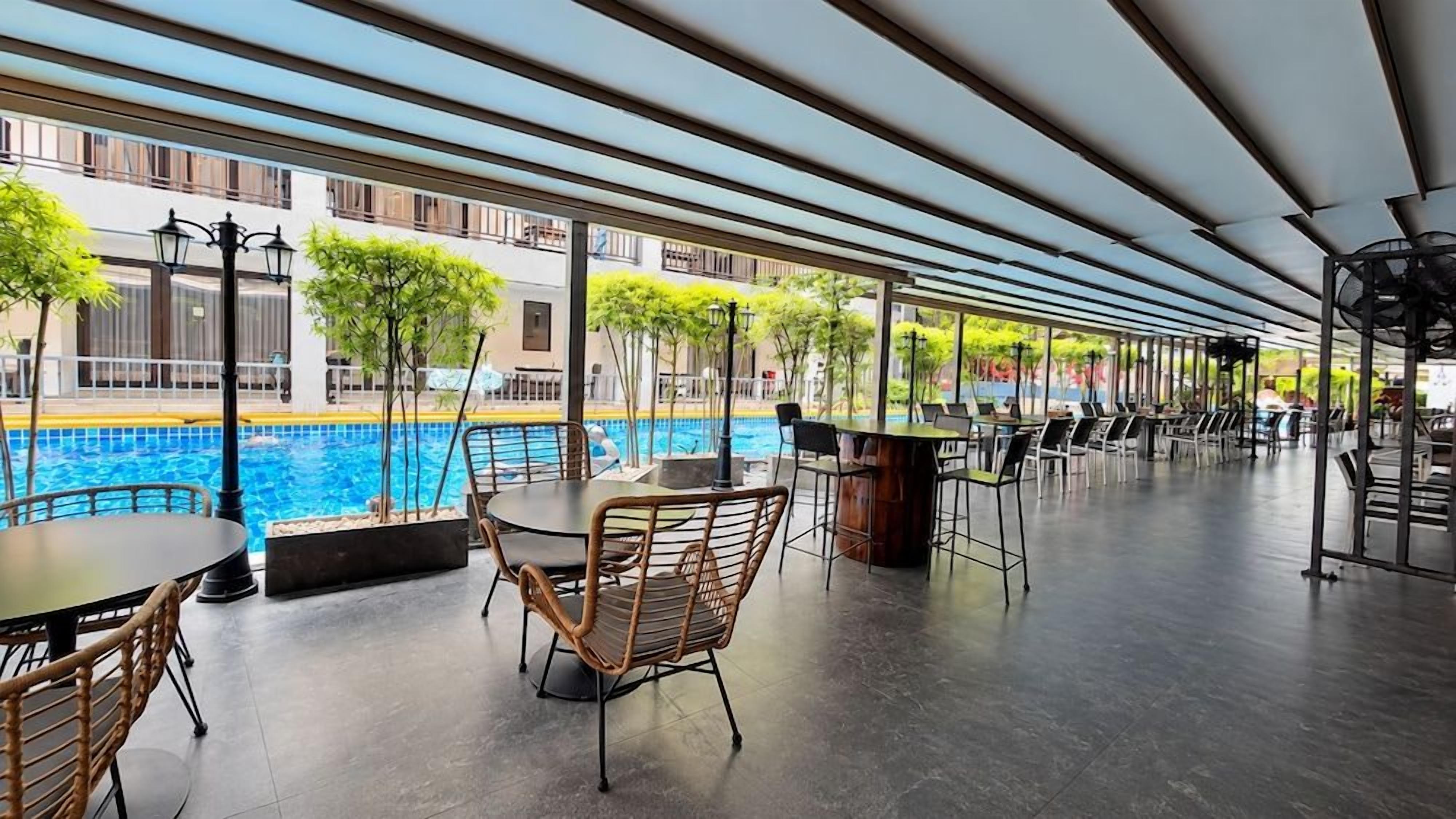 Área interna com piscina, mesas e cadeiras, vista de um edifício e uma galeria coberta.