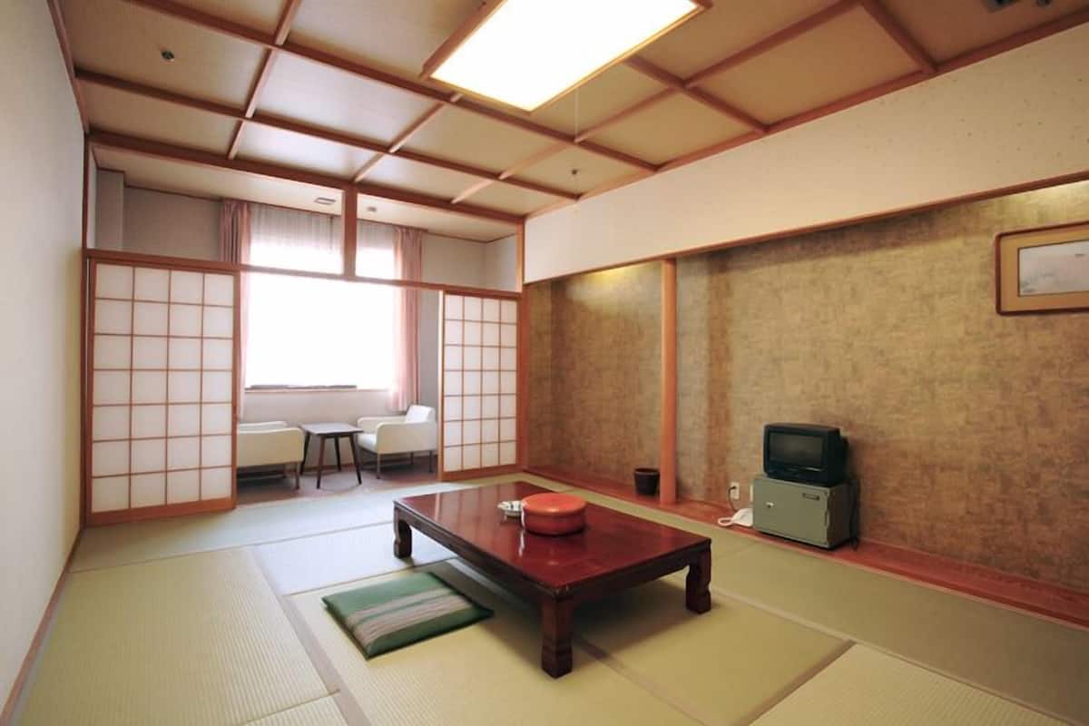 Quarto japonês tradicional com tatames, uma mesa de madeira baixa, uma televisão e uma porta de correr.