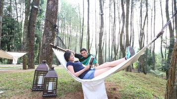 Uma rede em área arborizada com duas pessoas relaxando.