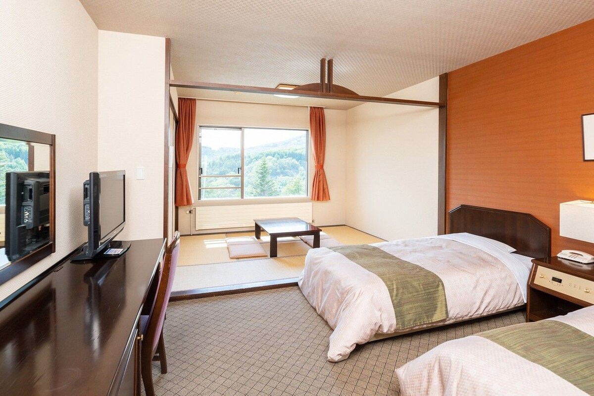 Quarto de hotel com duas camas, televisão, escrivaninha e janela com cortinas.