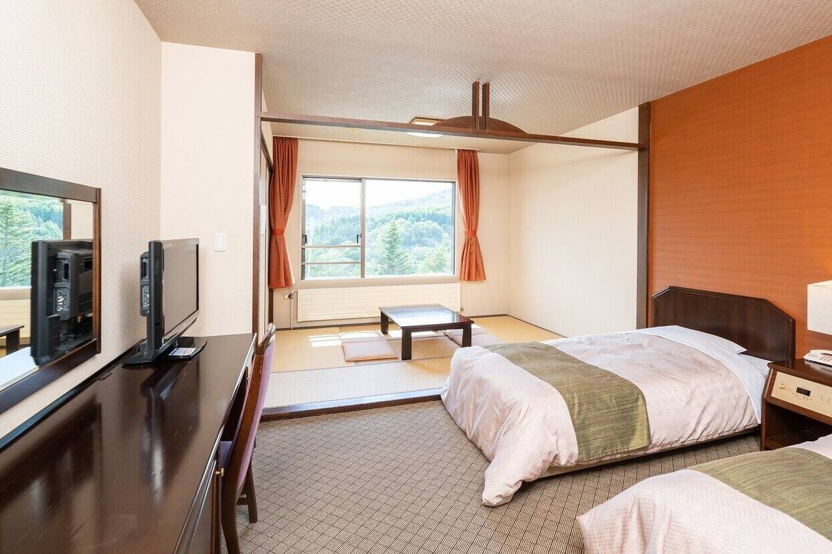 Quarto de hotel com duas camas, televisão, escrivaninha e janela com cortinas.