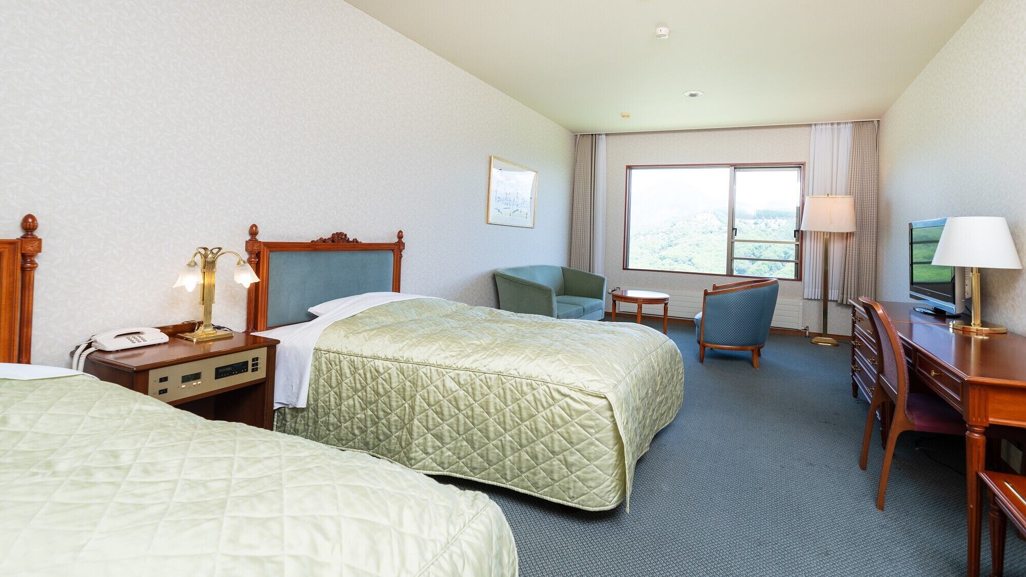 Quarto de hotel com duas camas, uma mesa, uma cadeira, uma televisão e uma janela com vista.