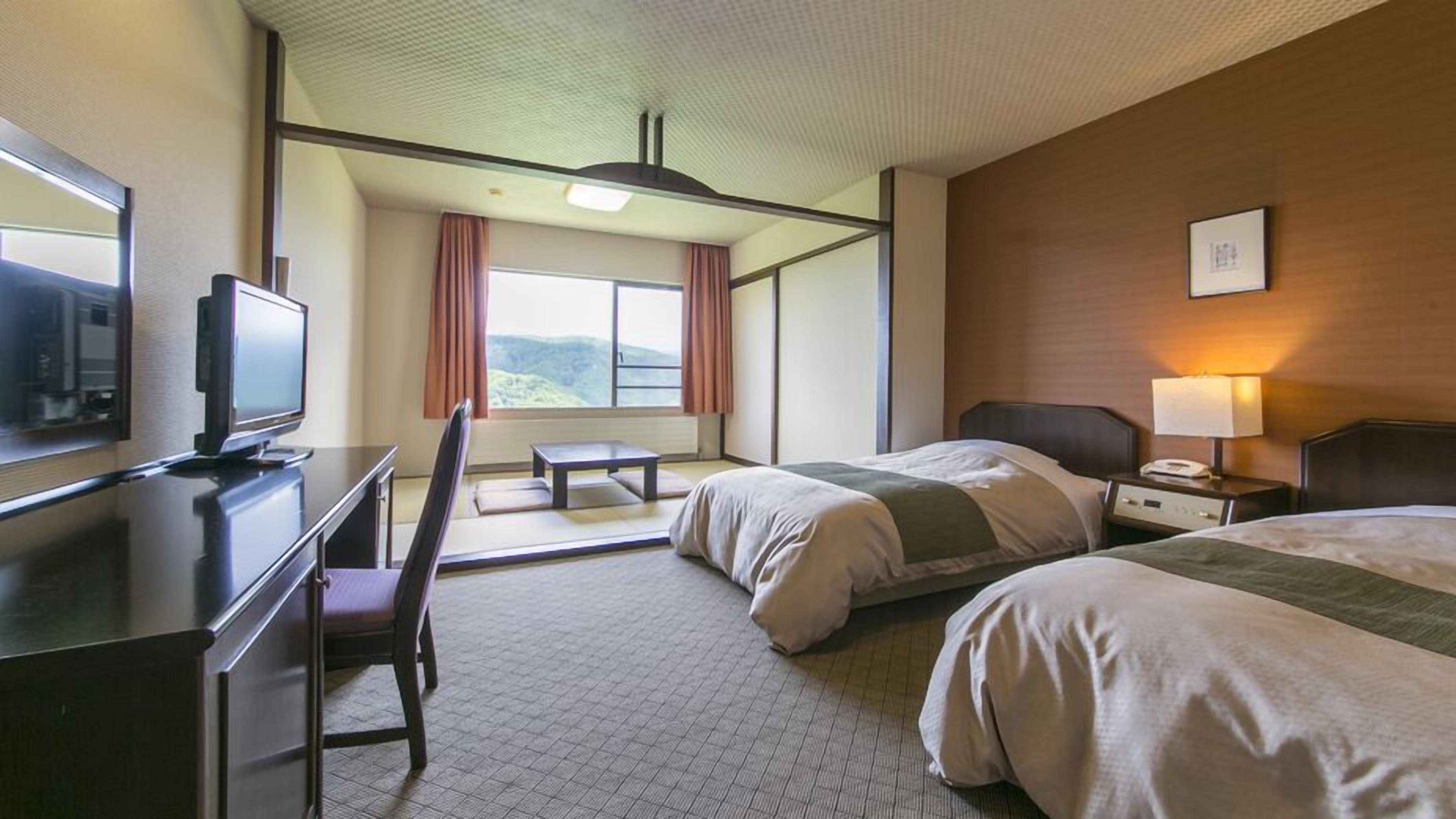 Quarto de hotel com duas camas, uma escrivaninha com cadeira, televisão, janela com cortinas e mesa de cabeceira com abajur.