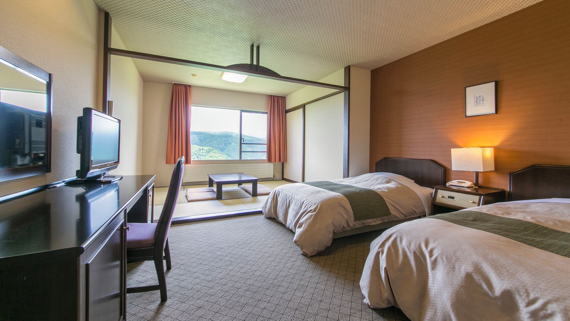 Quarto de hotel com escrivaninha, duas camas, televisão, janela com cortinas e luminária.