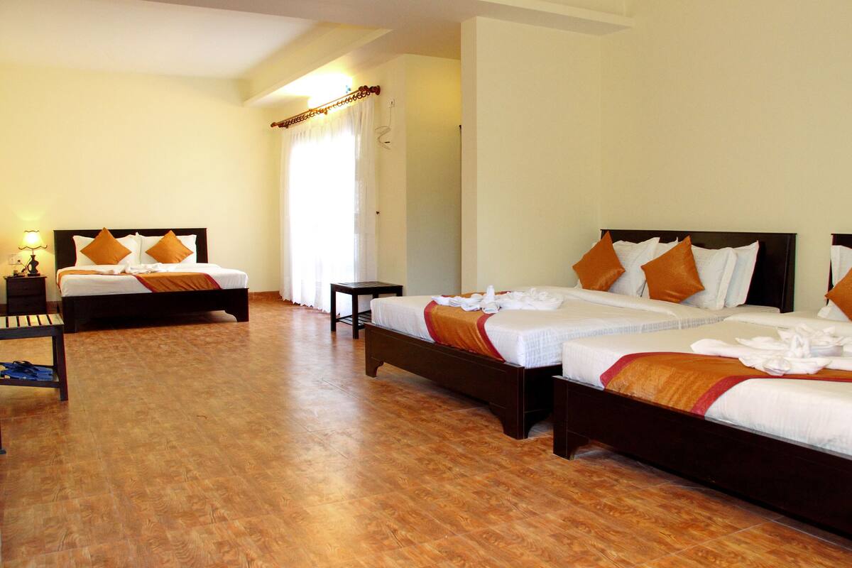 Quarto de hotel com duas camas de solteiro, uma mesinha e uma mesa de cabeceira.