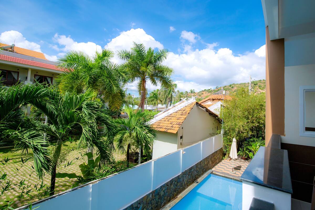 Vista da piscina com céu azul límpido, palmeiras e um edifício com telhado de azulejos.