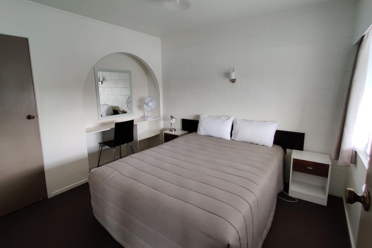 Quarto de hotel com uma cama grande, uma mesinha de vaidosa com espelho, uma escrivaninha e uma cadeira.