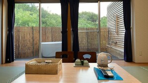 Quarto com porta de vidro deslizante para uma varanda, uma cesta de vime, uma mesa com chaleira e chávenas, e um comando à distância.