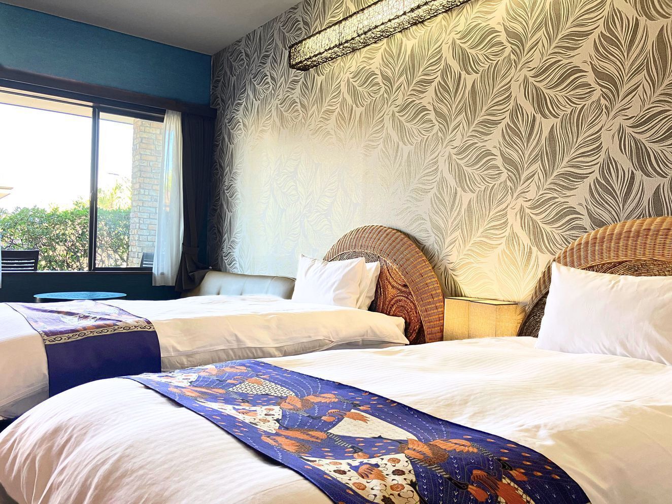 Quarto de hotel com duas camas, uma janela grande e parede com padrão.