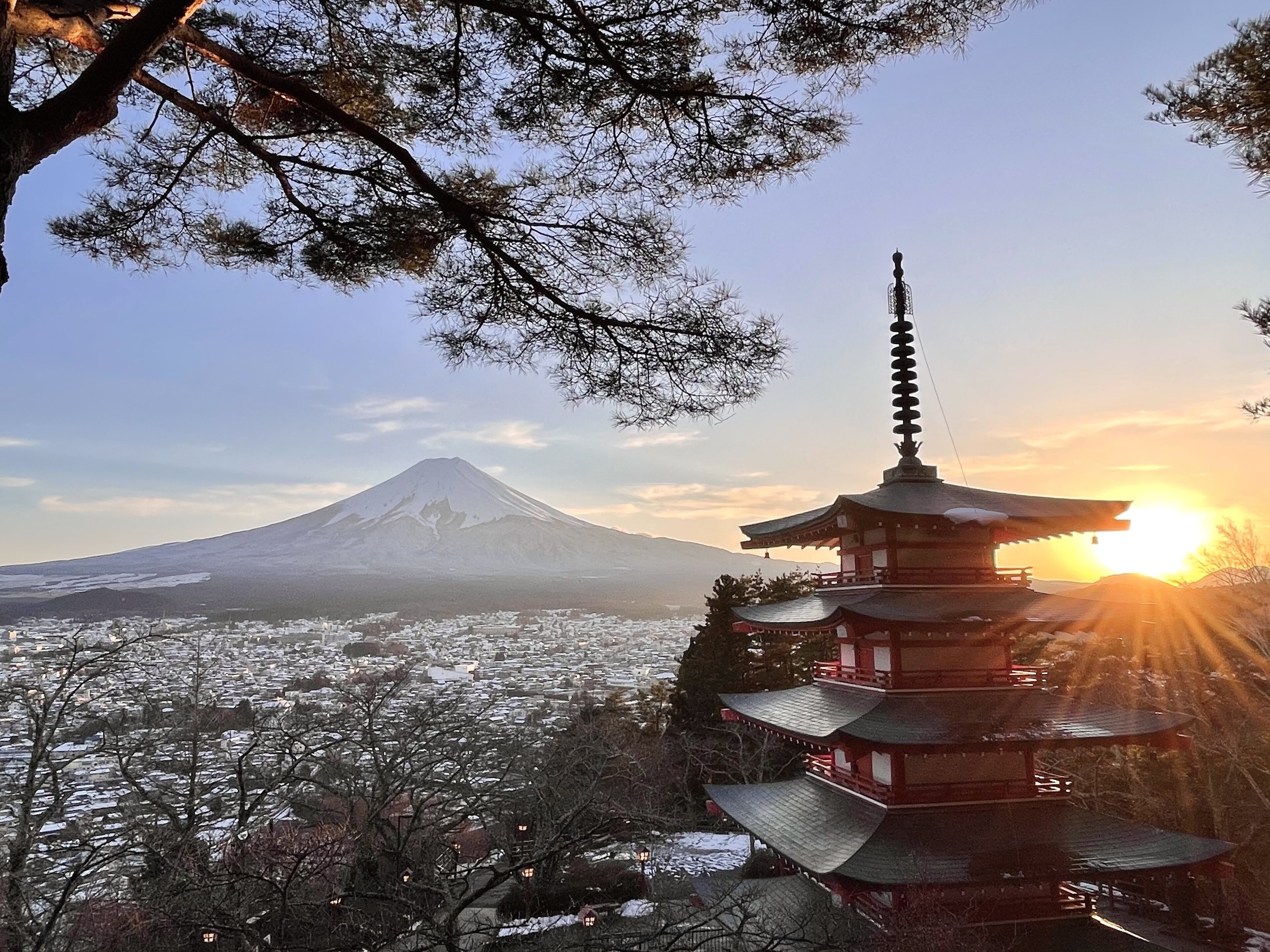 Uma pagoda com vários níveis, uma montanha coberta de neve ao fundo e uma paisagem urbana abaixo.
