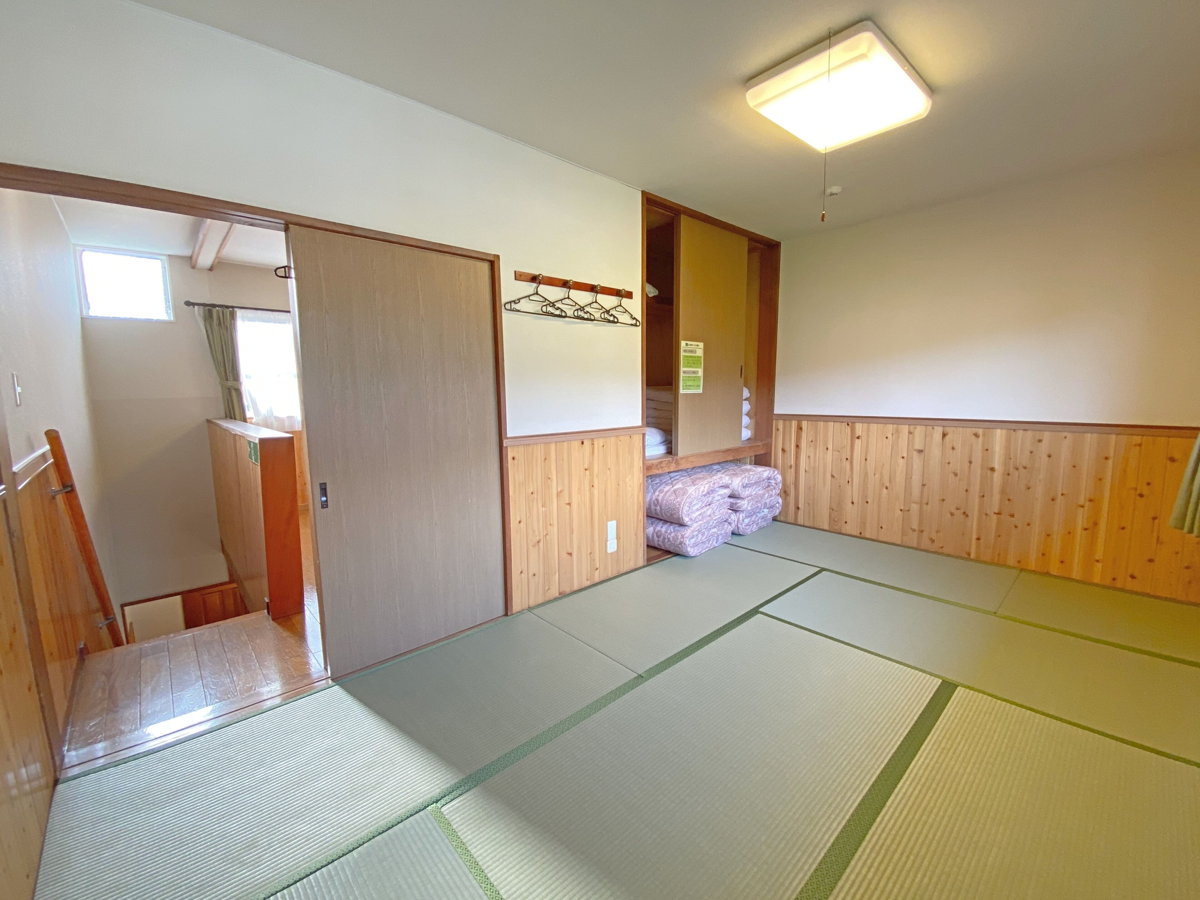 Um quarto com esteira de tatame, porta deslizante, prateleira de madeira e cabideiro suspenso.