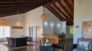 Ampla sala de estar com mesa de jantar, dois sofás, área de cozinha e ventilador de teto.