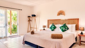 Quarto com uma cama grande, uma escada de madeira, uma mesinha com abajur e vista para o verde através de uma porta de correr.