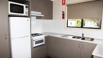 Uma cozinha compacta com micro-ondas, geladeira, fogão, forno e uma janela com vista para o verde lá fora.