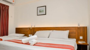 Quarto de hotel com uma cama grande, cabeceira de madeira, um quadro na parede e um toque de vermelho no edredom.