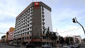 Um hotel com vários andares, um sinal vermelho e branco bem visível, diversas varandas e um restaurante no térreo.