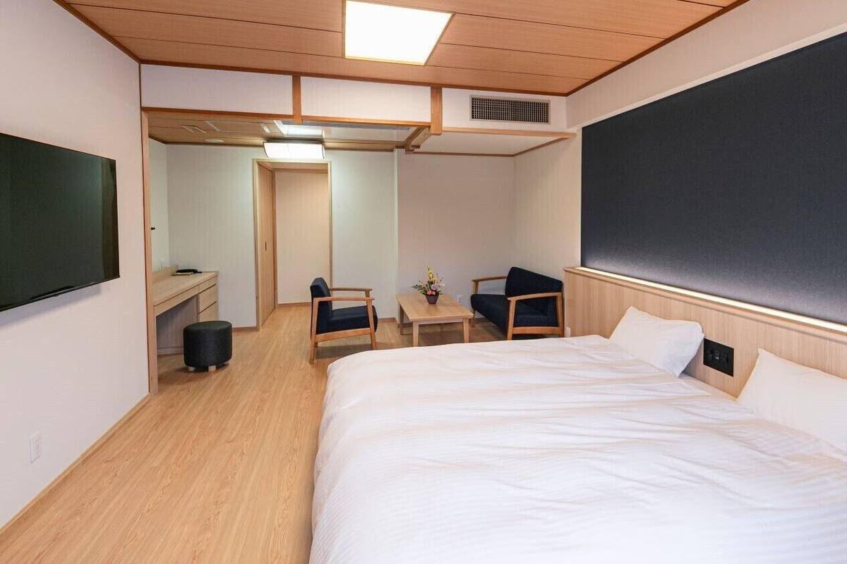 Quarto de hotel com uma cama grande, duas cadeiras, uma escrivaninha e uma televisão de tela plana.